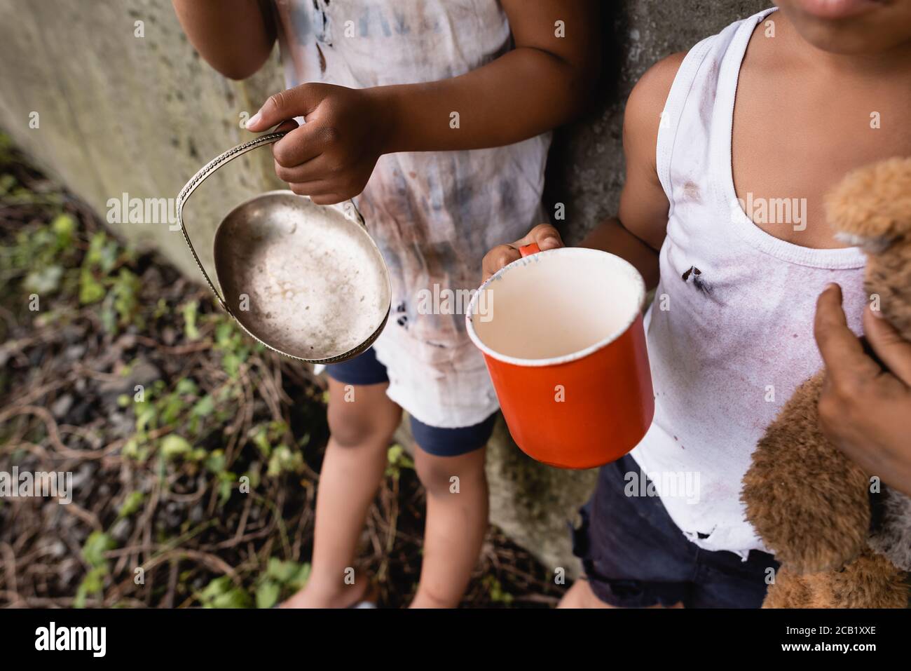 Cropped view of homeless african american kids holding cup and metal ...