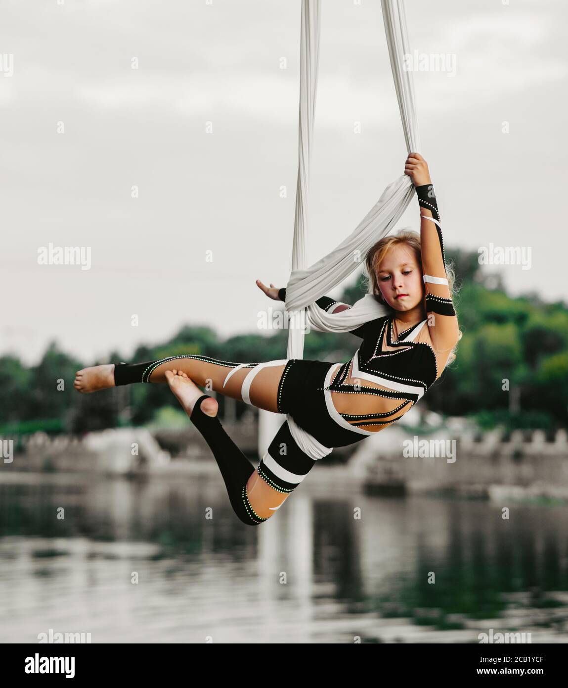 Child girl aerialist performs acrobatic tricks on hanging aerial silk ...
