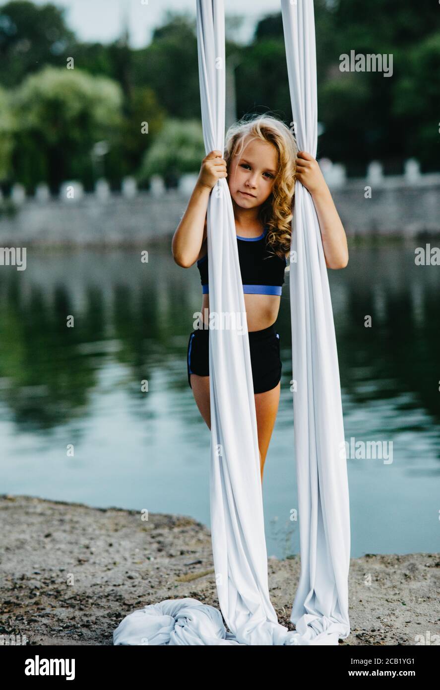 Child girl aerialist standing near hanging aerial silk against ...