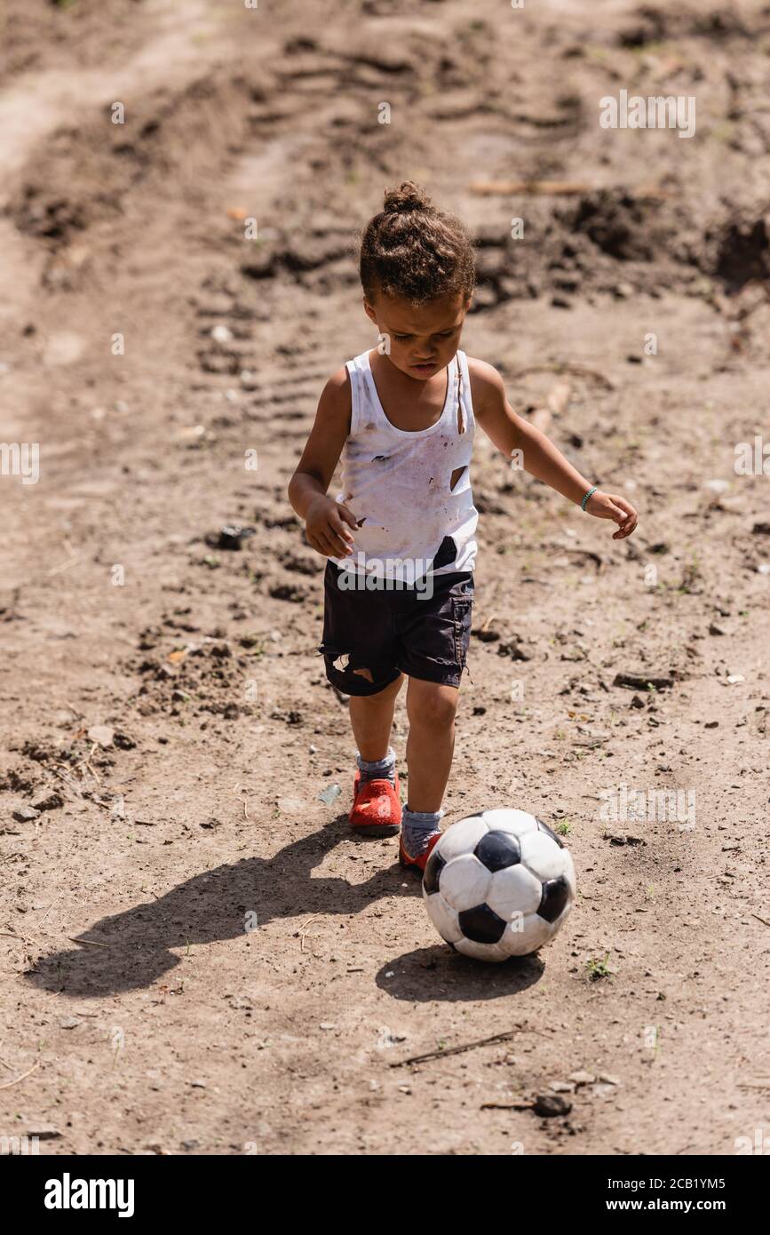 Poor african american boy playing football on dirty road on urban ...