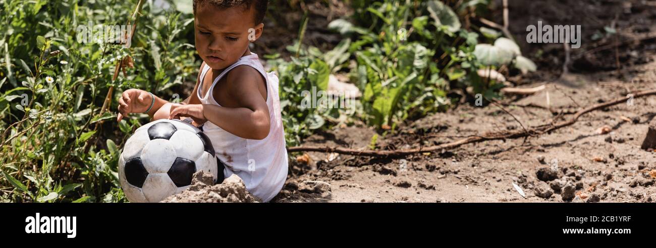 Panoramic crop of poor african american boy sitting near football on ...