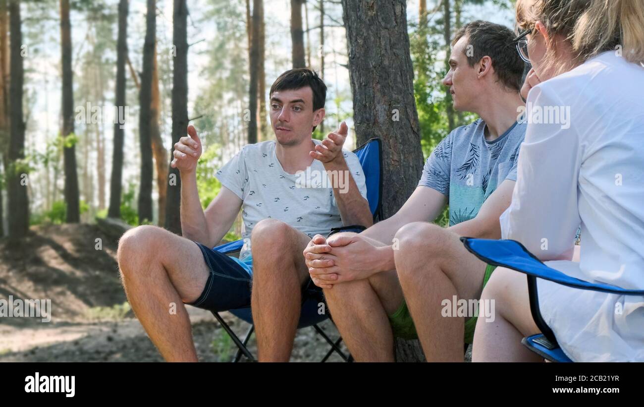 Group of friends sitting on chairs in a pine forest and communicate ...