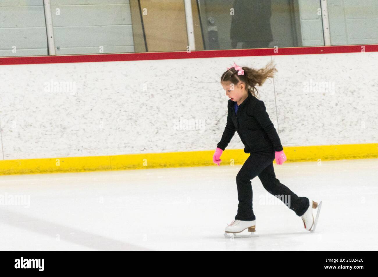 Little girl practicing figure skating moves on the indoor ice rink ...