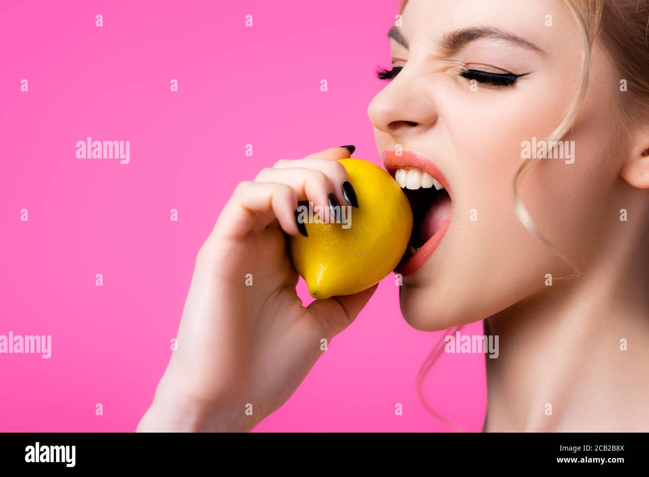 beautiful blonde woman biting ripe lemon isolated on pink Stock Photo ...