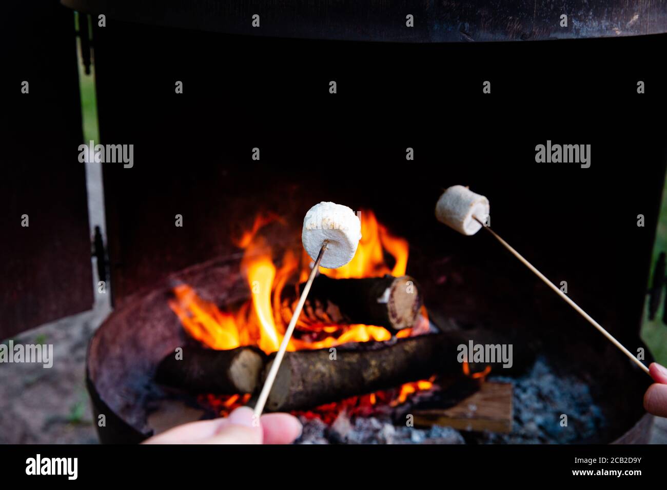 Person roasting over fire flames a marshmallows over campfire at night ...