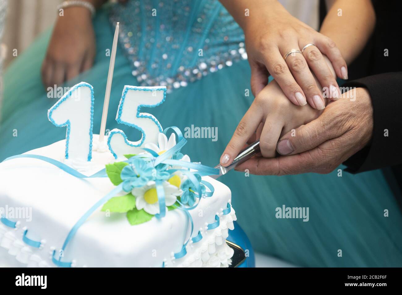 Parents are holding a young girl's hand while she is cutting her ...
