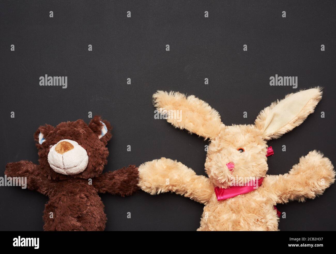 beige plush rabbit toy with long ears and a brown bear on a black ...