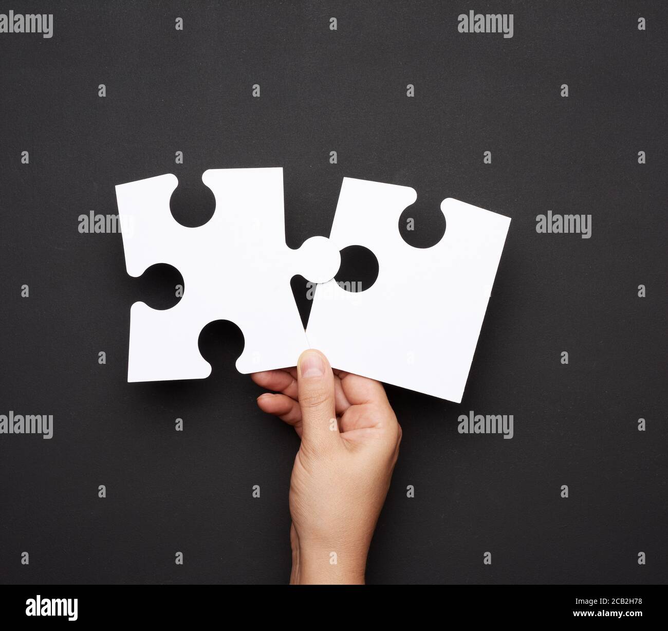 female hand holding big paper white blank puzzles on a black background ...