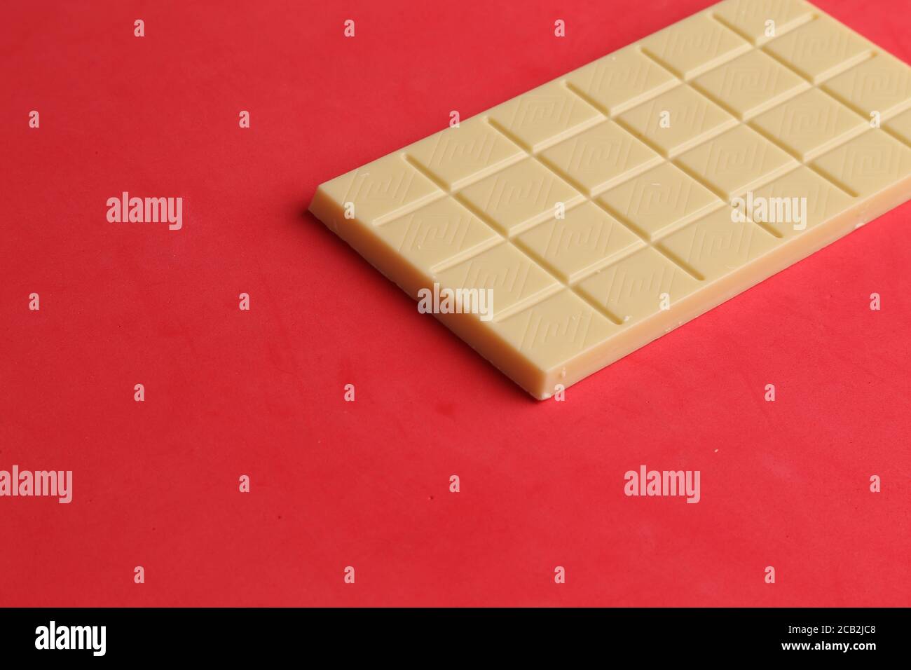 Flat long bar of white chocolate on a red surface Stock Photo - Alamy