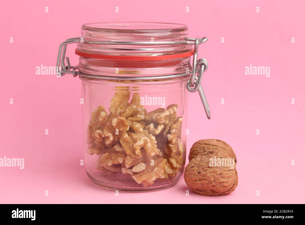 Closeup of walnut kernels inside a jar with two whole walnuts on the ...