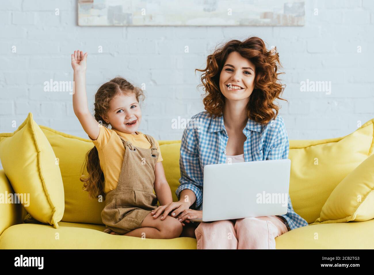 happy child waving hand and young nanny smiling at camera while sitting ...