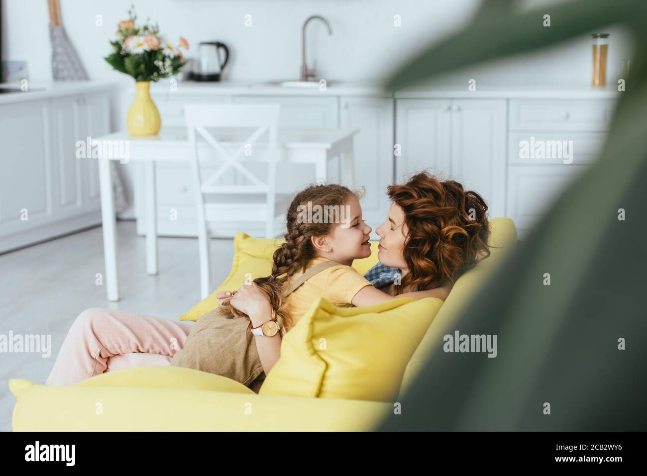 selective focus of cute kid hugging happy nanny sitting on sofa in ...