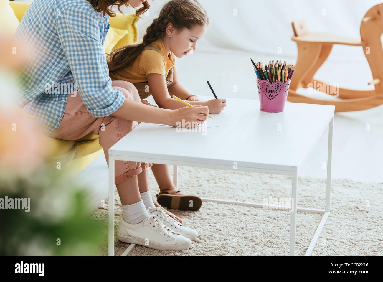 cropped view of nanny and child drawing with pencils, selective focus ...
