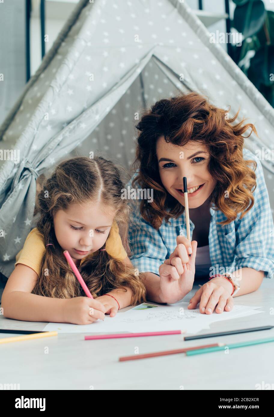 happy nanny with felt pen smiling at camera while lying in toy wigwam ...