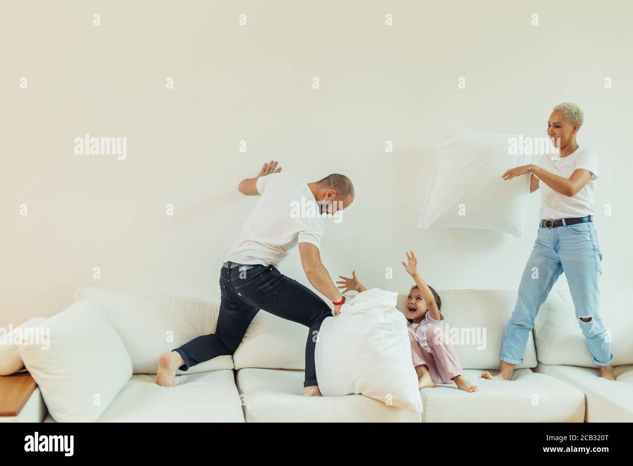 Happy joyful family fighting pillow battle on bed at home with children ...