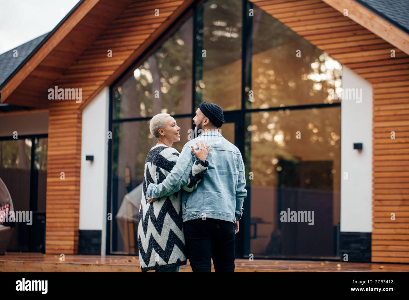 Caucasian woman and man stand hugging next to big house in countryside ...