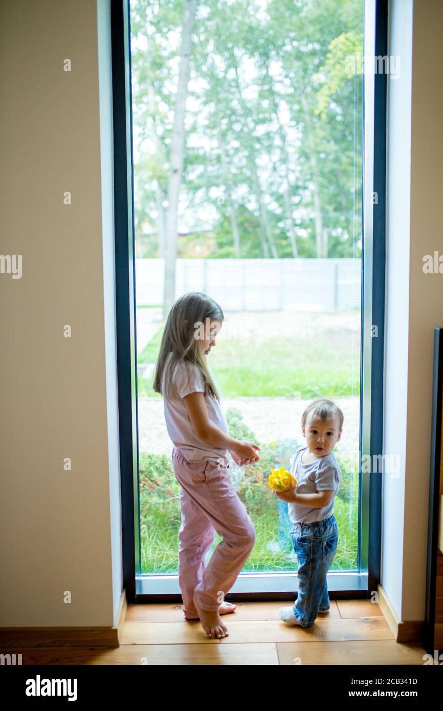 Children standing near panoramic window at home, baby surprisingly look ...