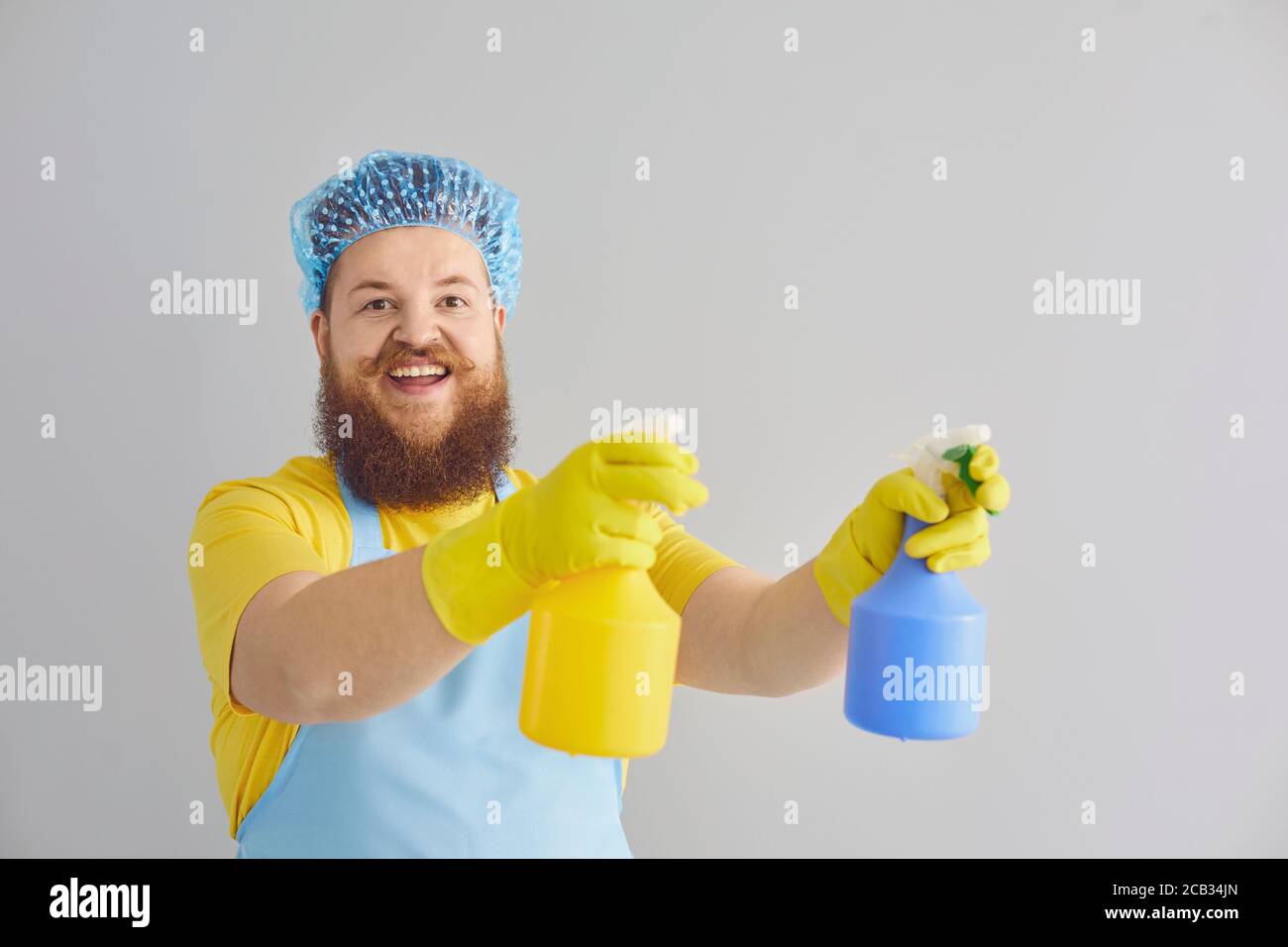 Funny smiling red bearded male cleaner in cap and apron disinfecting ...
