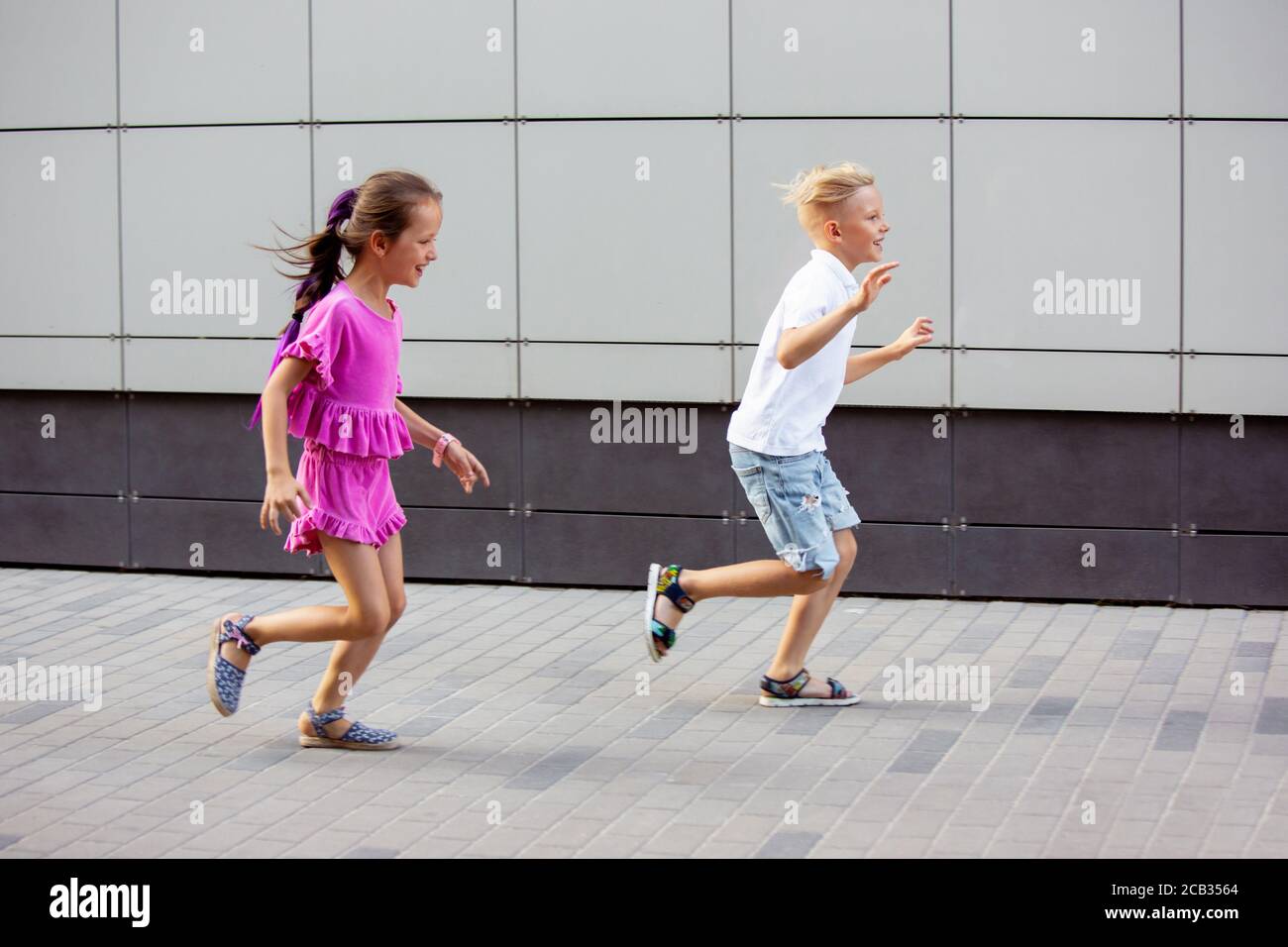 Summer eve. Two smiling kids, boy and girl running together in town ...