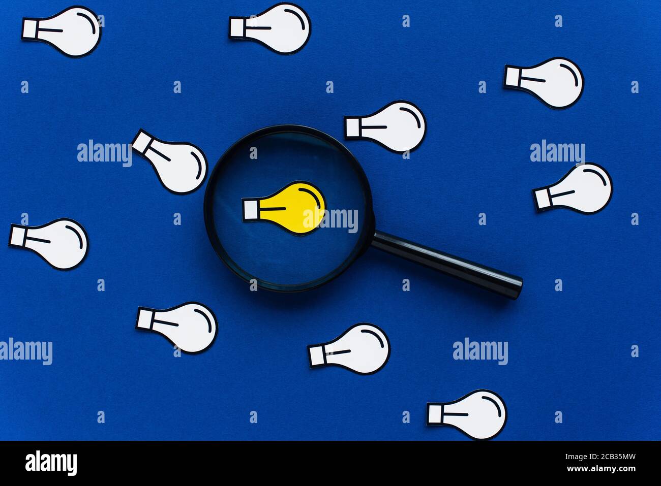 top view of paper light bulbs and magnifying glass on blue background ...