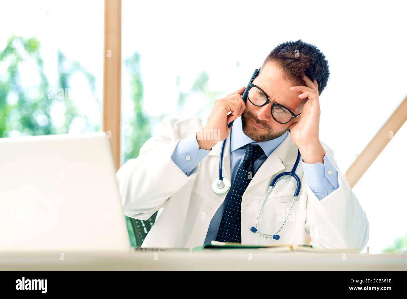 Shot of stressed male doctor sitting at desk behind his laptop and ...