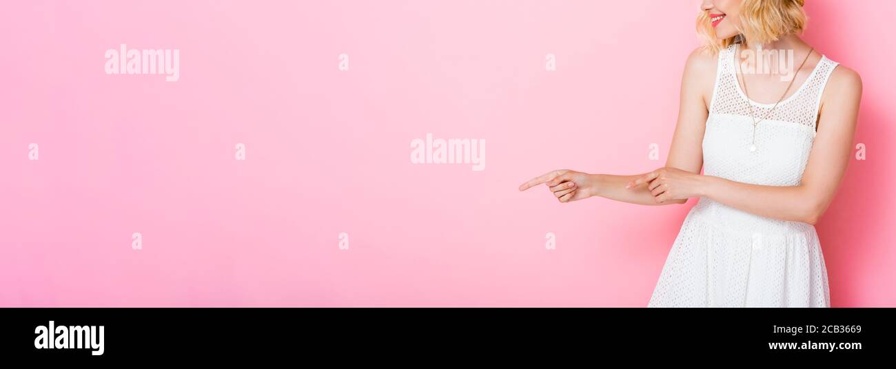 panoramic crop of woman in white dress pointing with fingers on pink ...