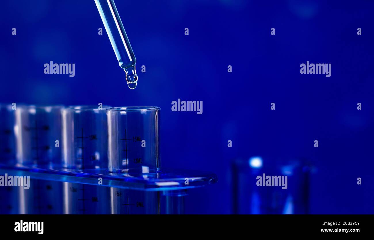 A drop is falling from an eyedropper into a test tube on a blue ...