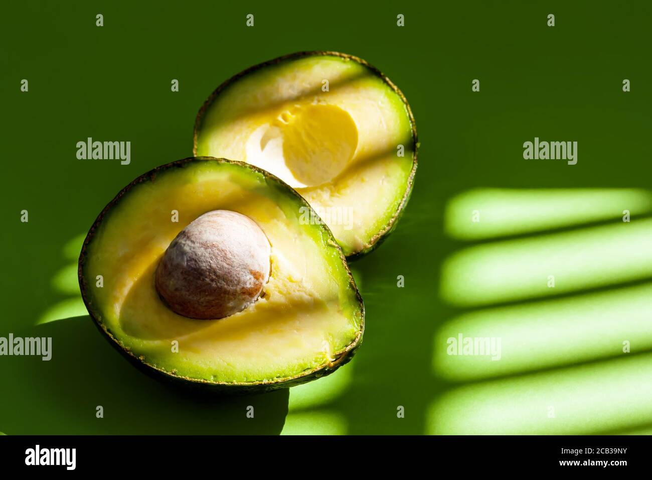 Fresh ripe avocado cut in half on the green background with shadows of ...