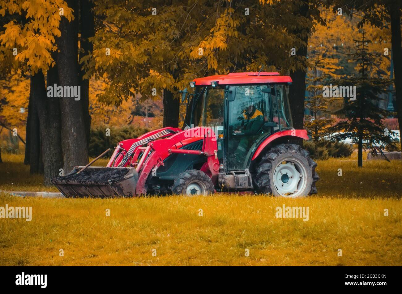 Small red tractor in the autumn park transport the pots with flowers ...