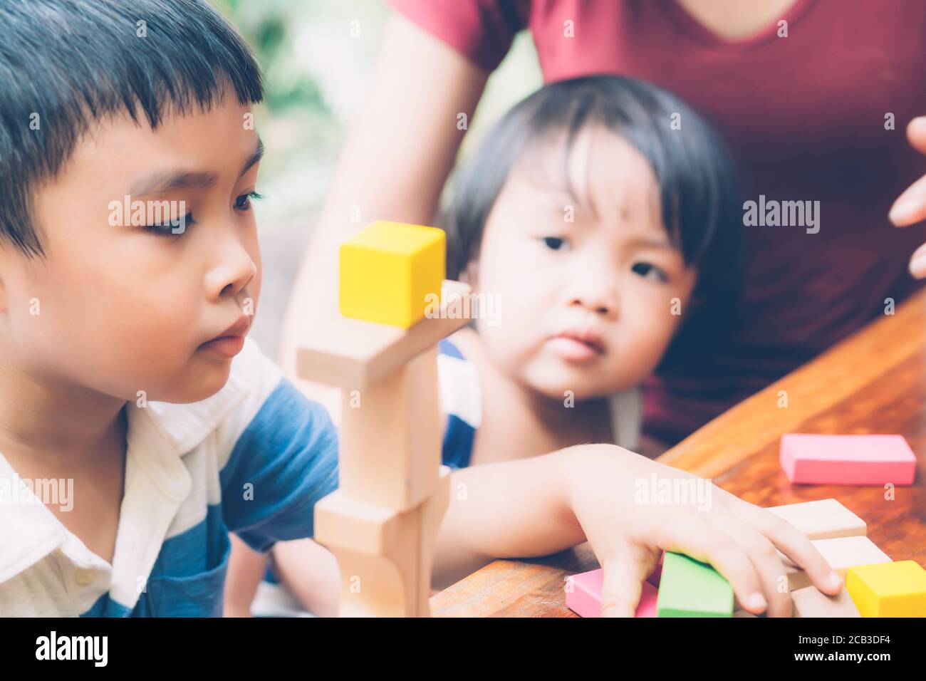 Family with asian mother and children playing toy block at home, mom and son and daughter doing ...