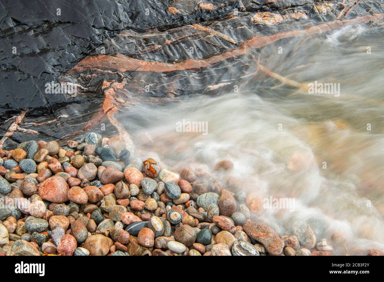 Beach pebbles and rock face with igneous intrusion on Lake Superior ...