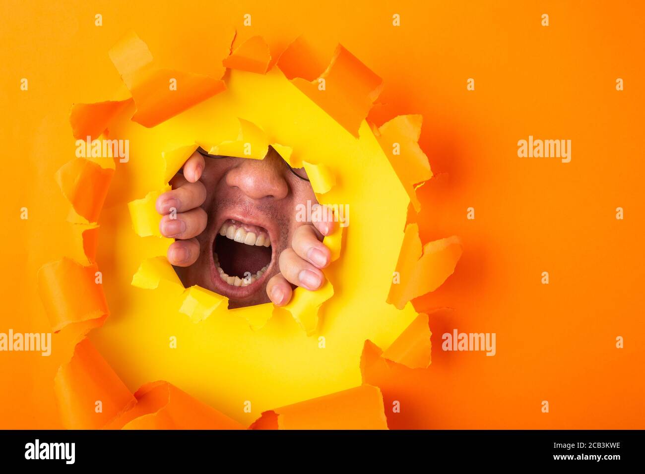 Angry male screaming out from behind hole of orange paper Stock Photo ...