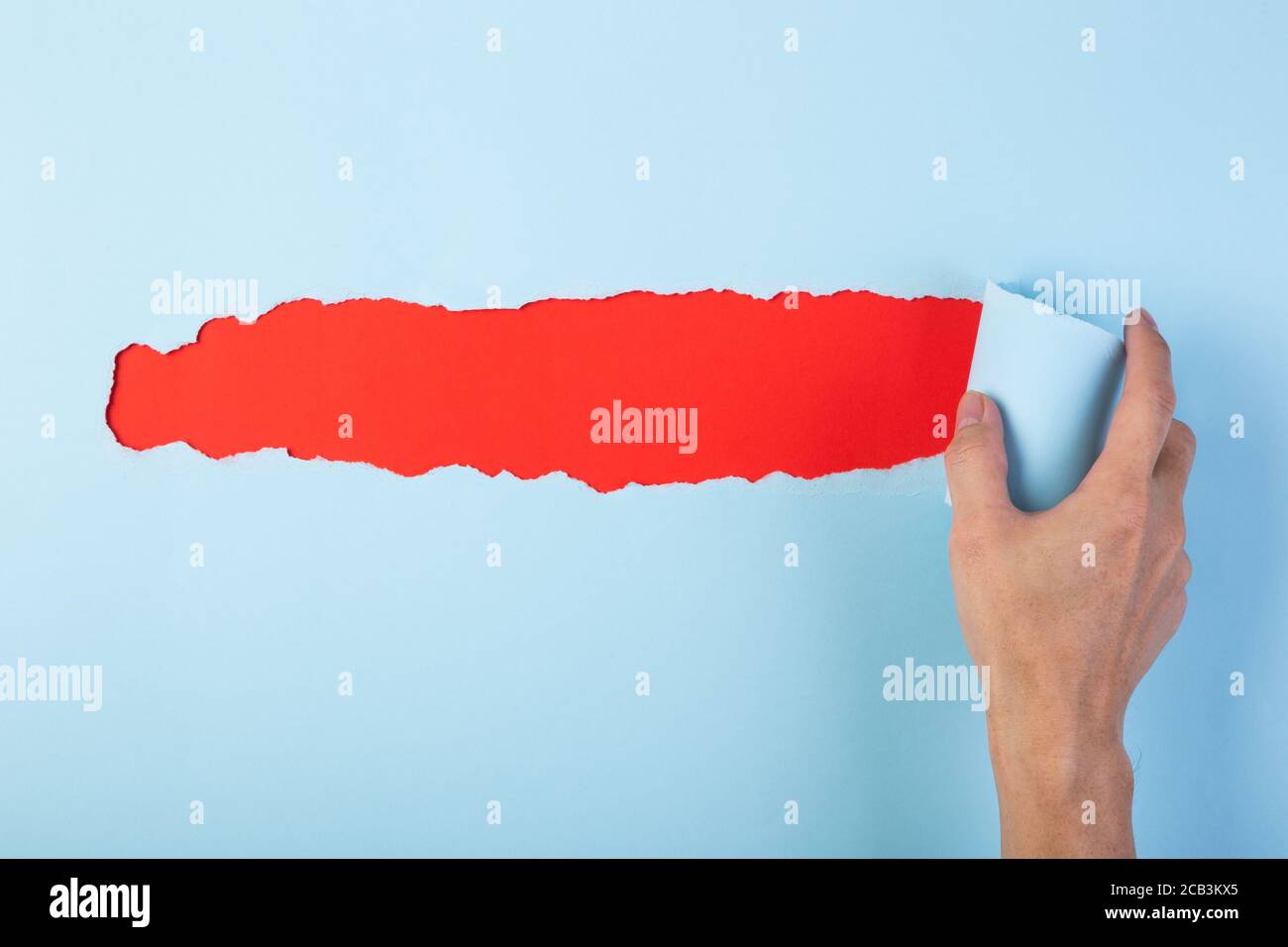 Person's hand tearing color paper background revealing copy space Stock ...
