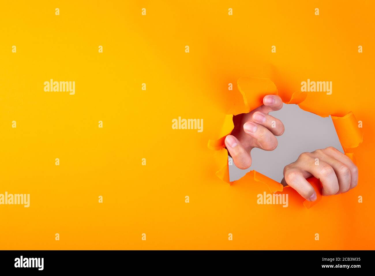 Person's hands ripping a hole in an orange paper with torn edges Stock ...