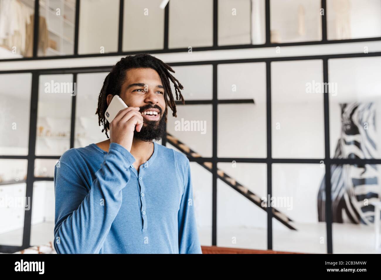 Cheerful young african man using mobile phone while standing in the ...