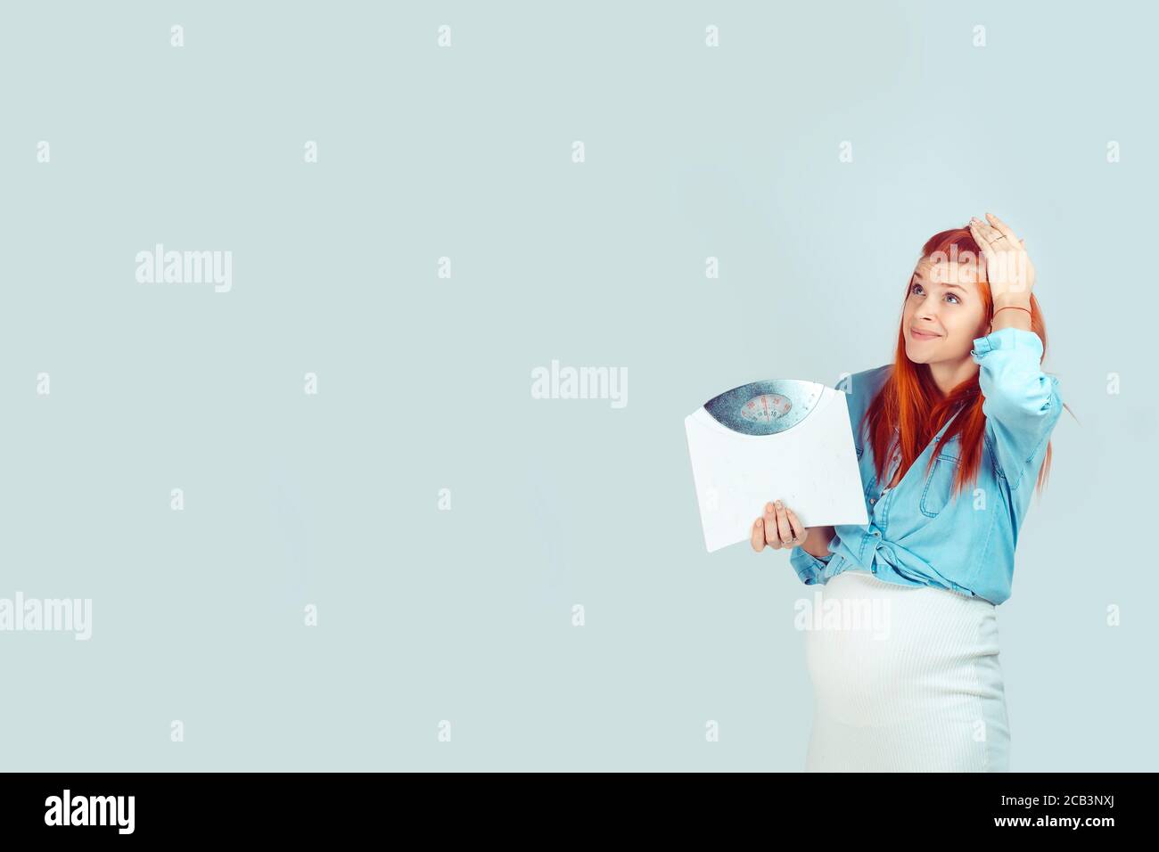 Young scared pregnant woman having overweight and holding weight scales ...