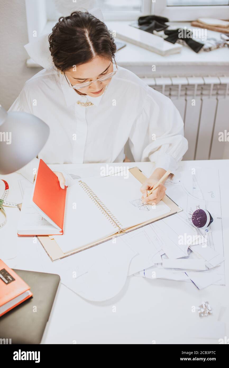 young woman designer in white shirt write in a notebook, creating new ...