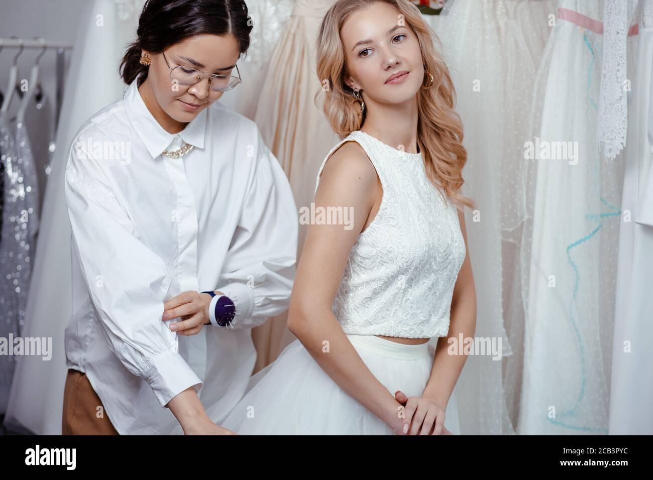 beautiful caucasian woman client and tailor in wedding boutique, taking ...