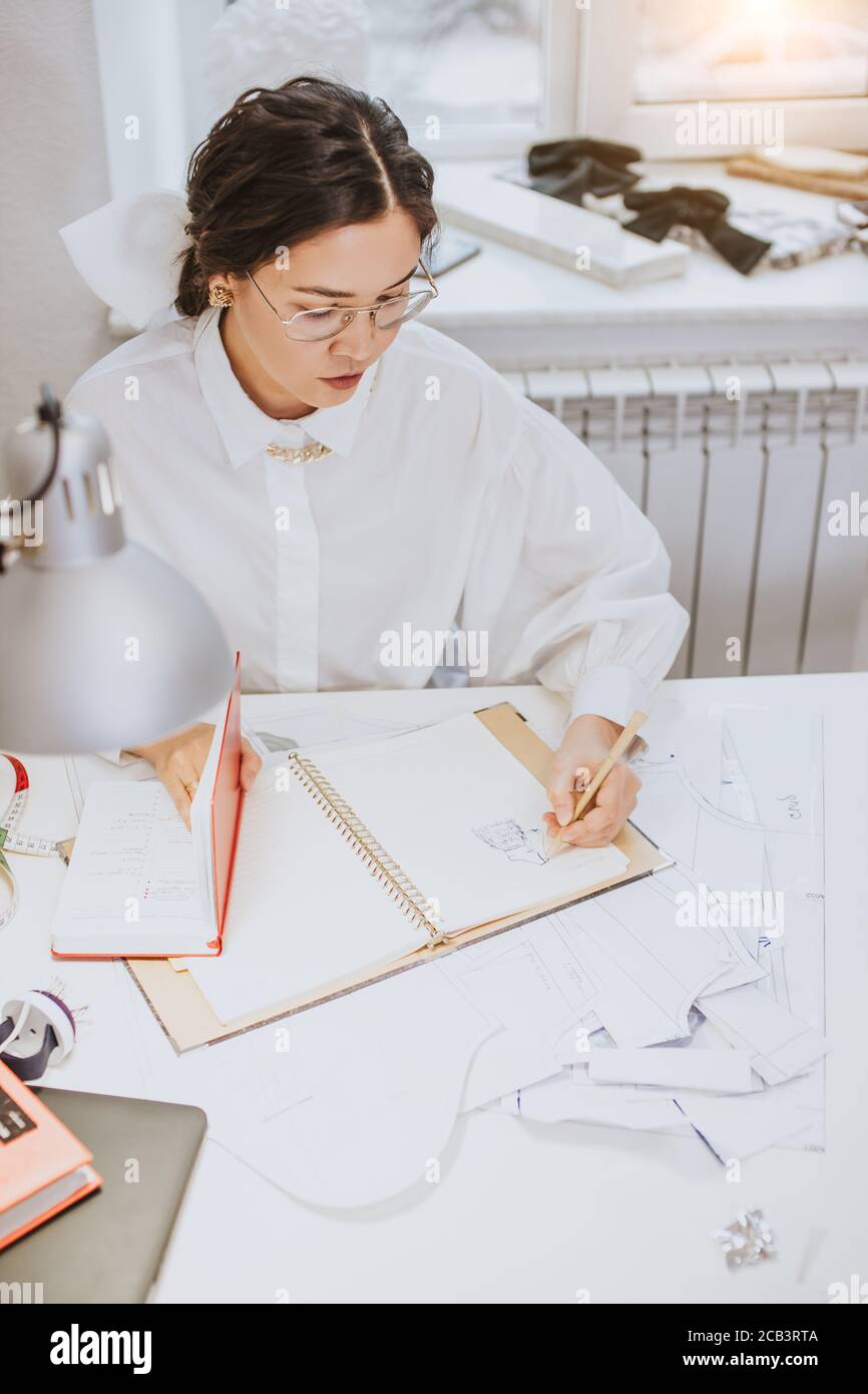 young and beautiful female designer busy at work, sit with notebook ...