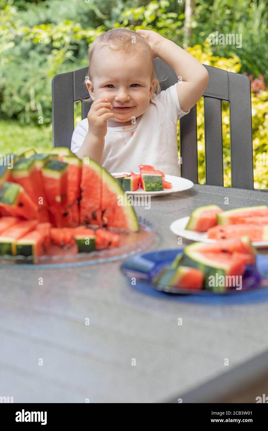 Cute baby boy is dirty from eating watermelon sitting at a table ...