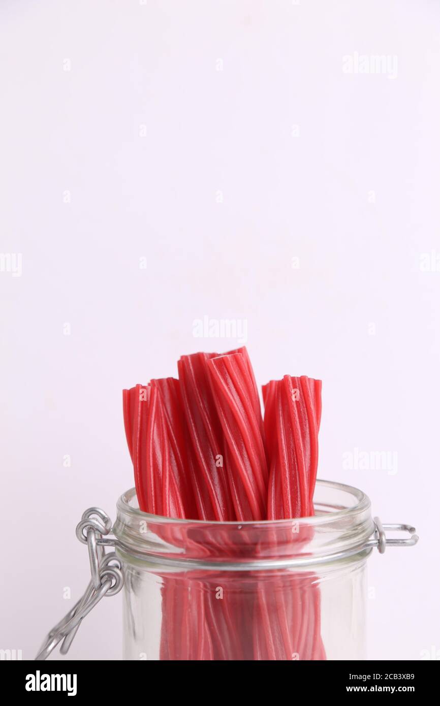 Vertical shot of glass jar with red licorice sticks on a white ...