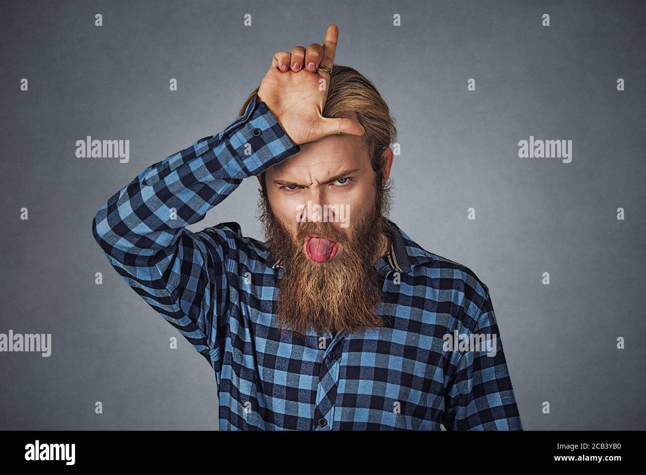 Portrait of a funny young bearded man holding finger up at his forehead ...