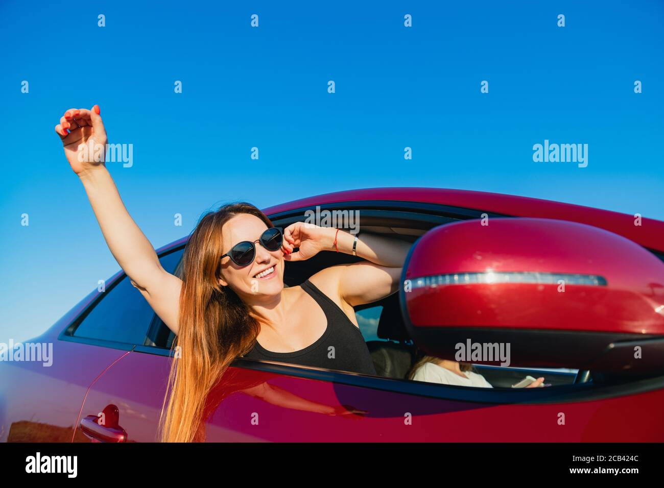 Young female in sunglasses put out hand and body from red vehicle at ...
