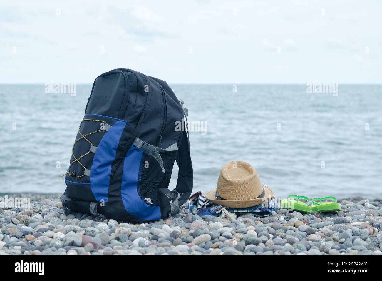 Backpack, hat and clothes on the pebble beach. Sea in the background ...