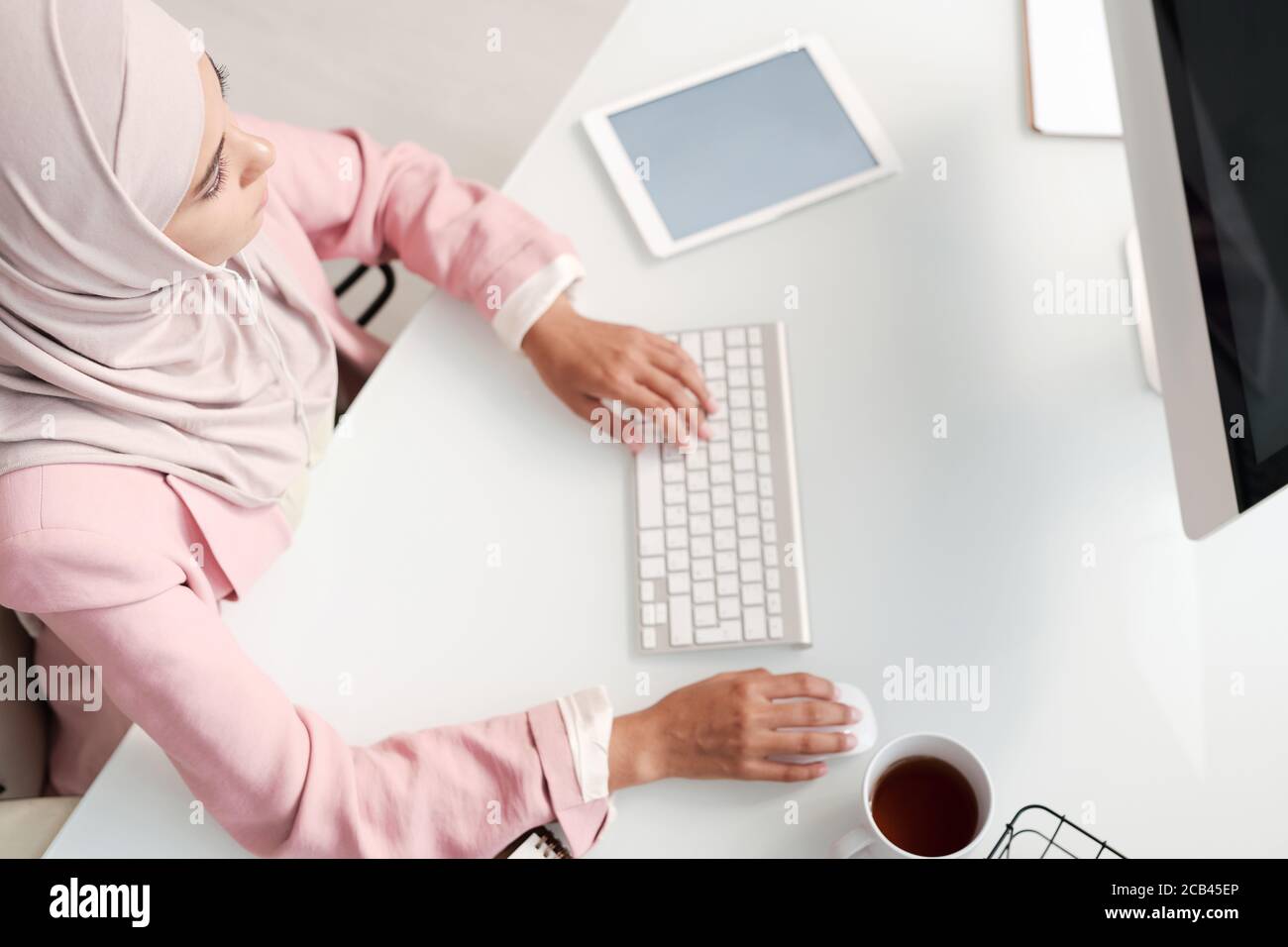 Above view of busy young Muslim woman in hijab sitting at desk and ...