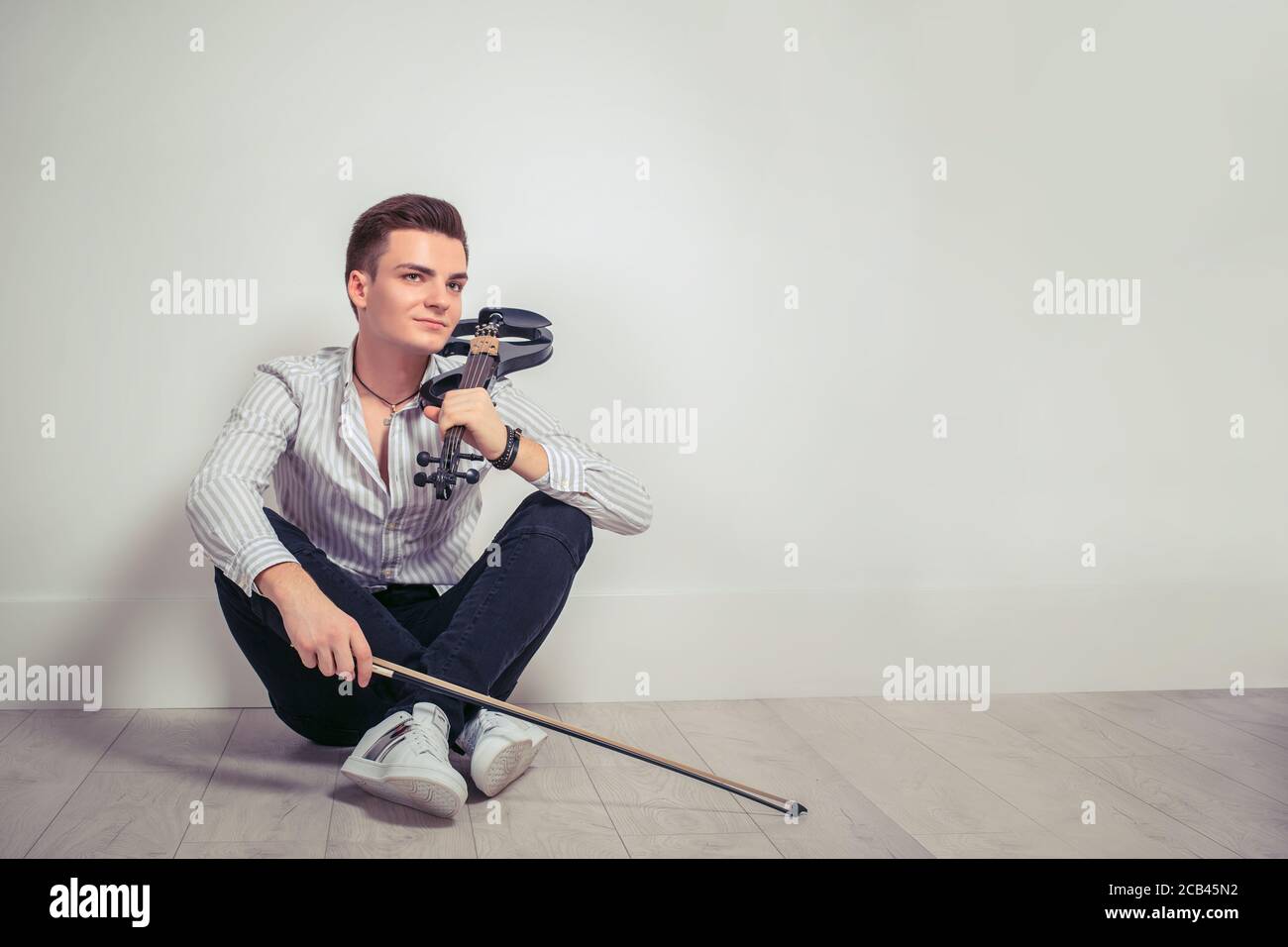 Handsome young man in shirt and denim holding violin and fiddle while ...