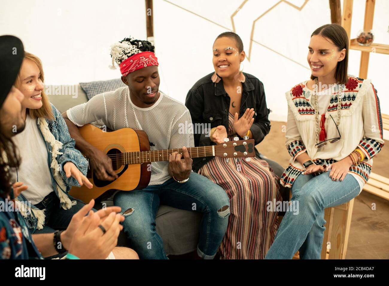 Positive young black musician playing guitar and singing song with ...