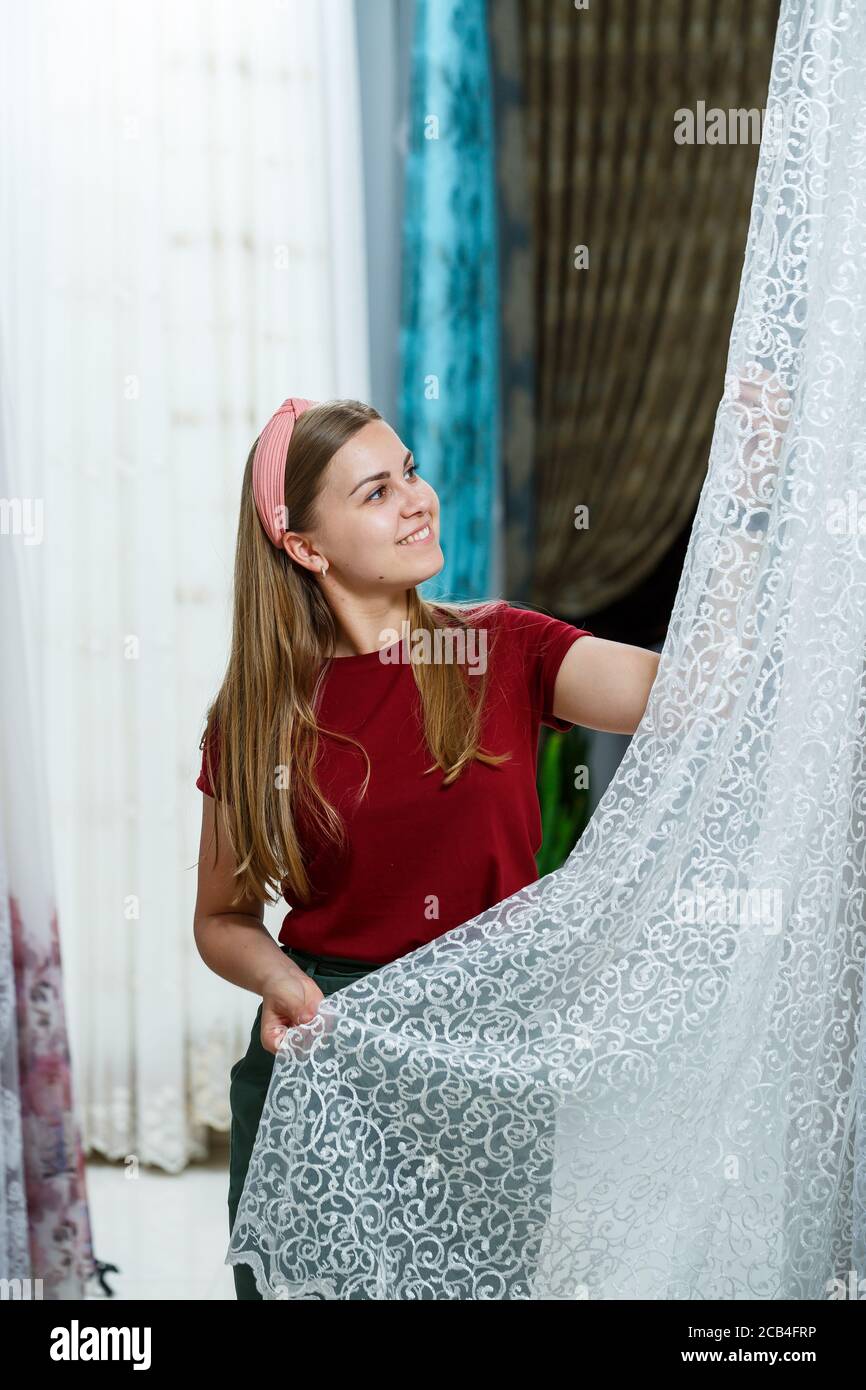 Young woman choosing fabric for new curtains in a store. Samples of the ...