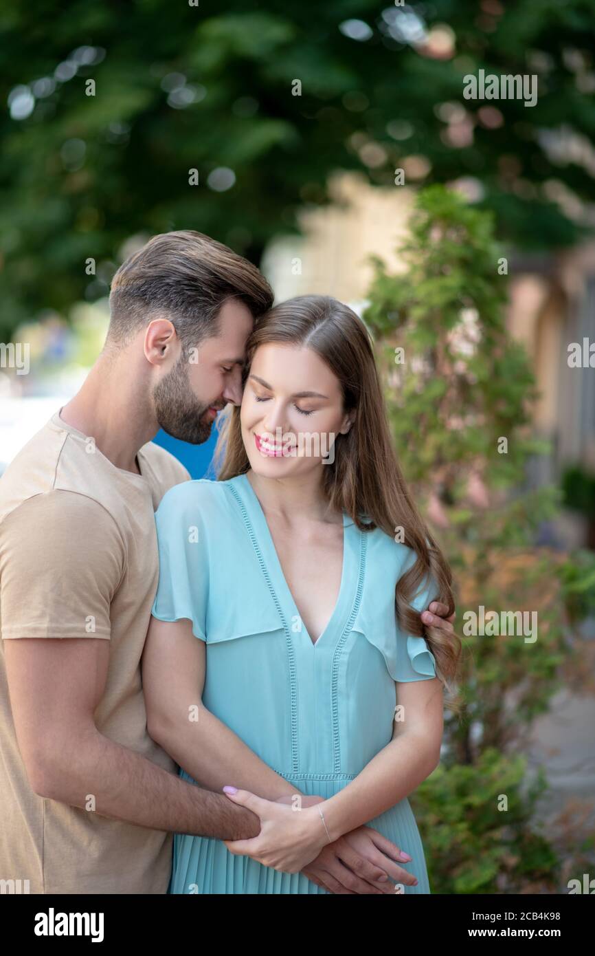 Bearded male hugging tenderly female in blue dress, pressing his forehead to her face Stock ...