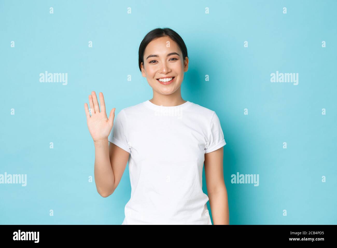 Portrait of friendly cheerful asian girl in white t-shirt saying hello ...